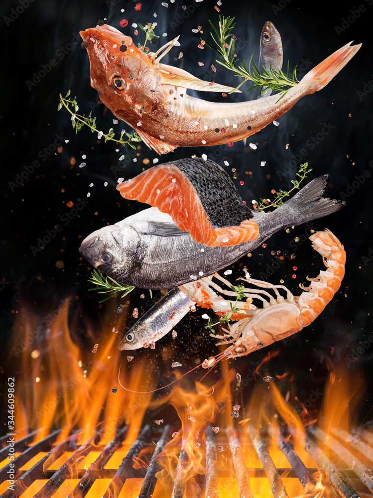 Tasty fishes flying above cast iron grate with fire flames. Freeze ...