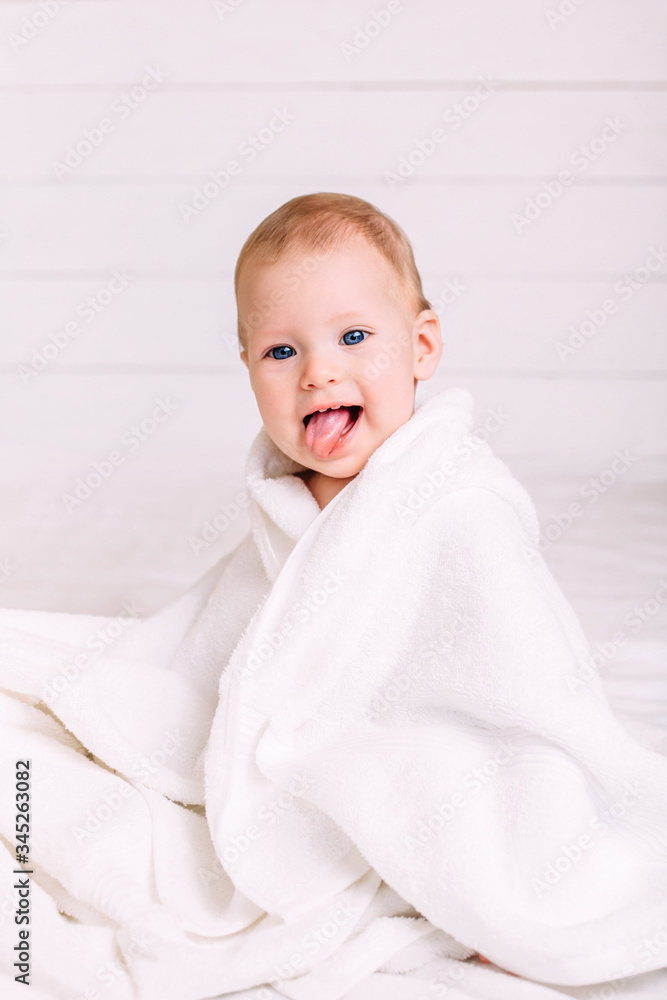 A cute baby with blue eyes wrapped in a white towel looks at the camera ...
