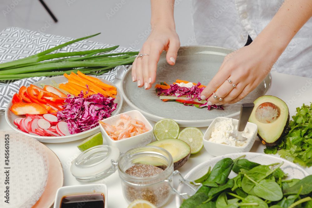 Woman's hands adding red cabbage and cheese to the spring roll on rice ...