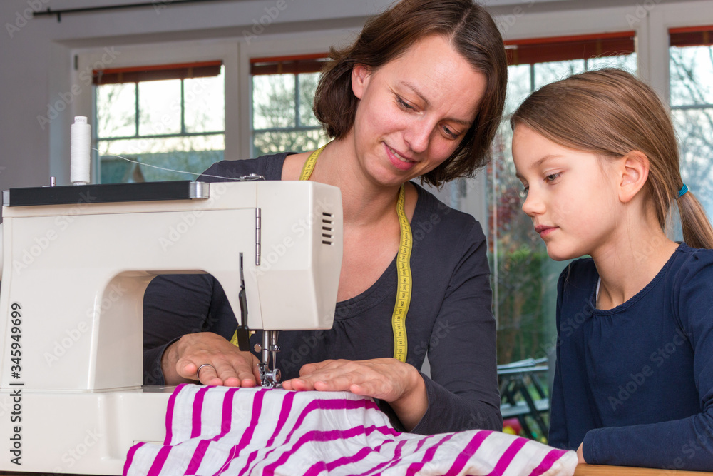 Mother teaches her 8 year old daughter how to sew a striped textiles ...
