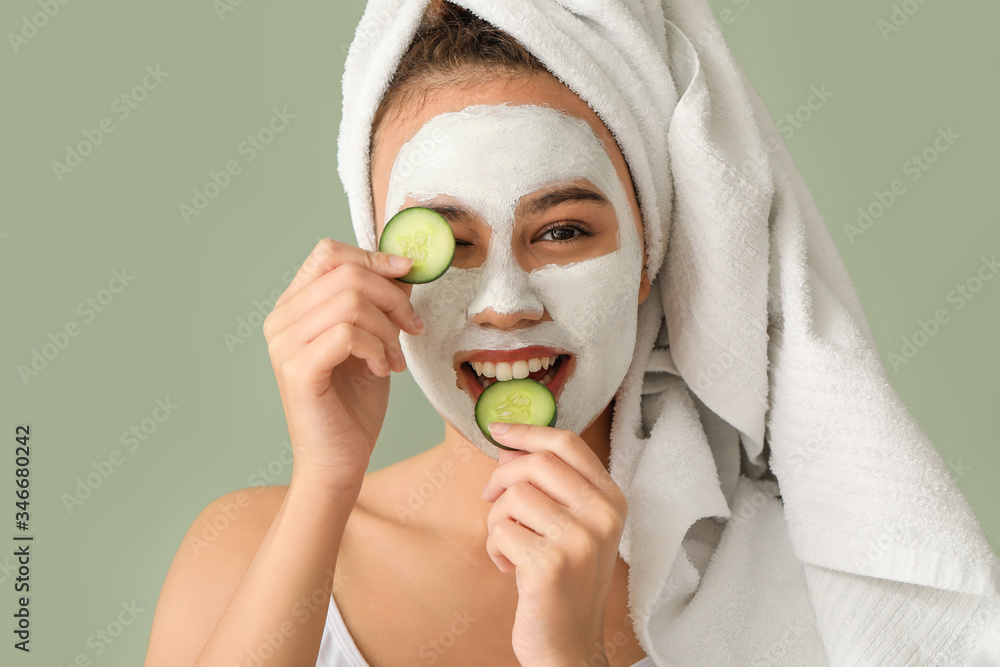 Beautiful young African-American woman with cucumber slices and facial mask on color background ...