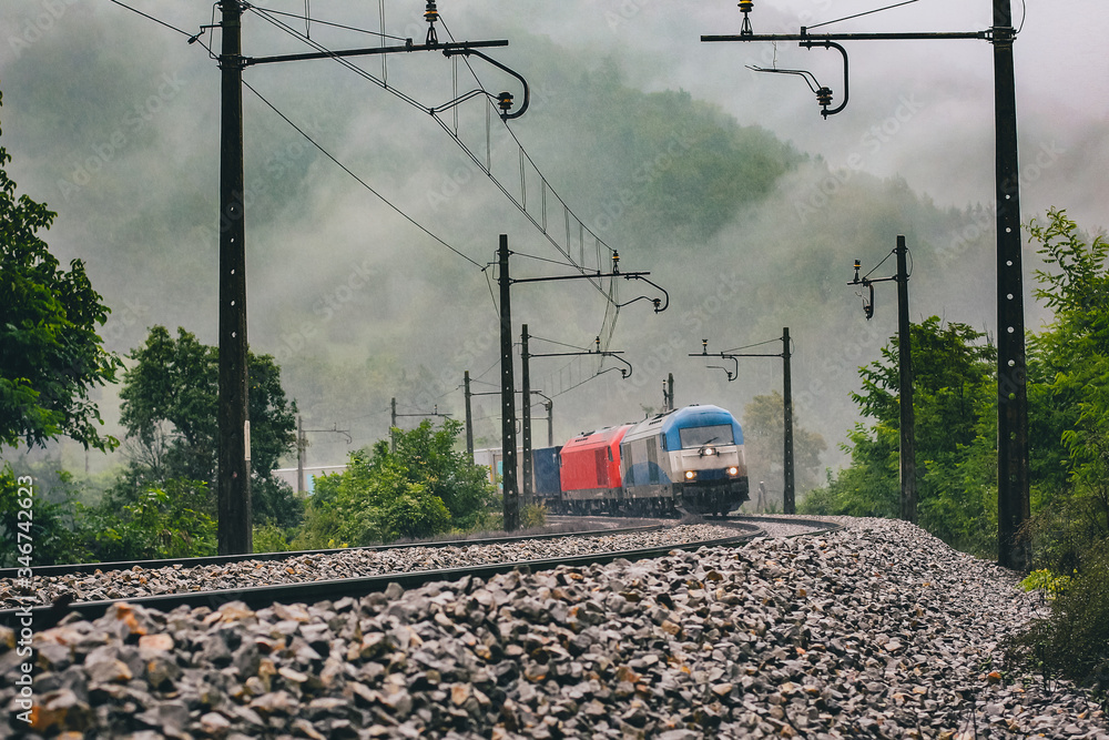 Silver and blue diesel locomotive pulling a freight train in rainy ...