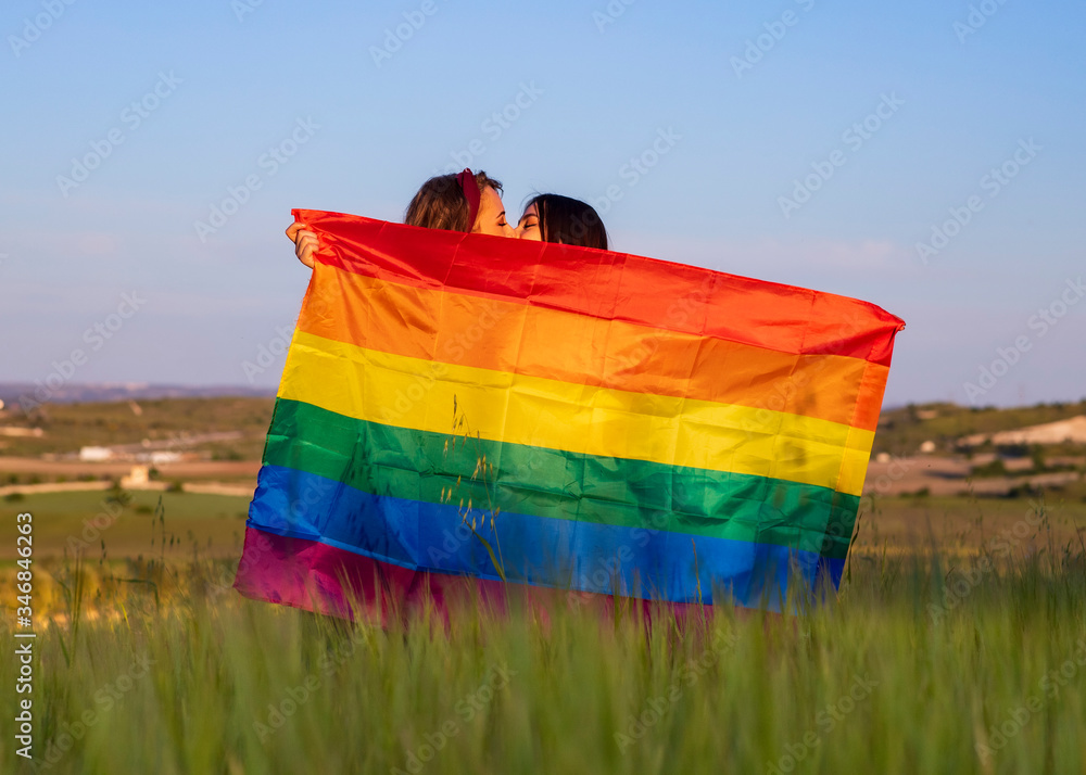Beautiful young lesbian couple kissing gently with the rainbow flag ...