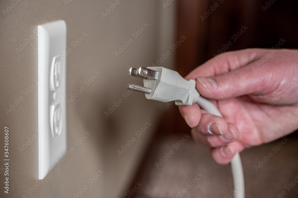 Caucasian hand gripping a three pronged power cord to insert into a ...
