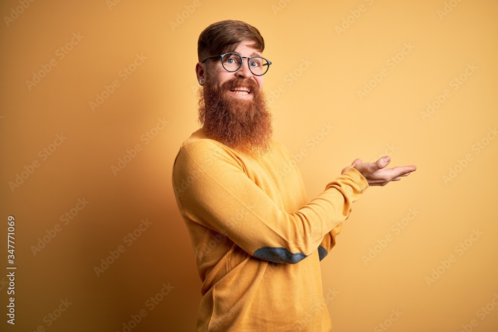 Handsome Irish redhead man with beard wearing glasses over yellow ...