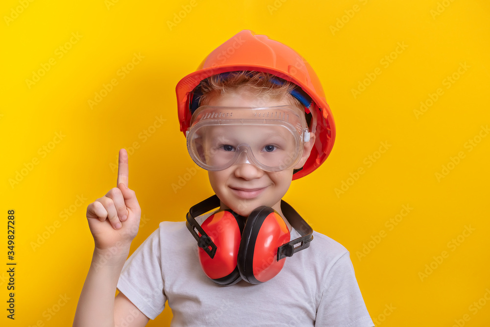 Cute boy in builder glasses, helmet and headphone to ear protection ...