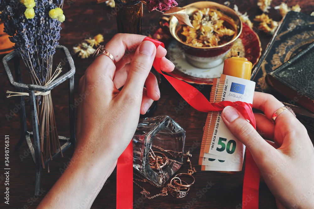 Wiccan witch casting money spell at her altar - tying red ribbon around ...