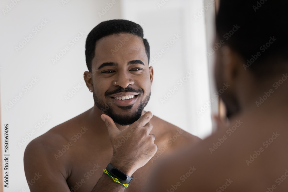 Foto Smiling young african American man look in mirror in bathroom ...