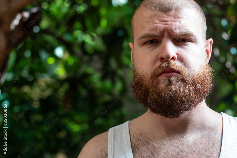 Bearded bald man in an undershirt with hairy chest standing outside ...