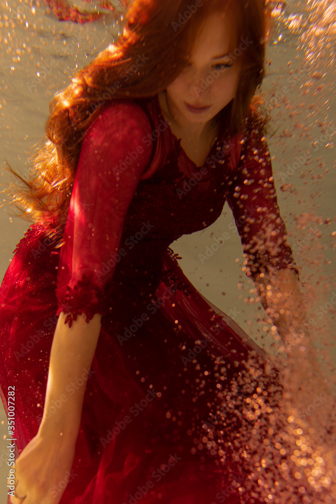 Beautiful girl underwater in a red dress swims in the pool. Tenderness ...