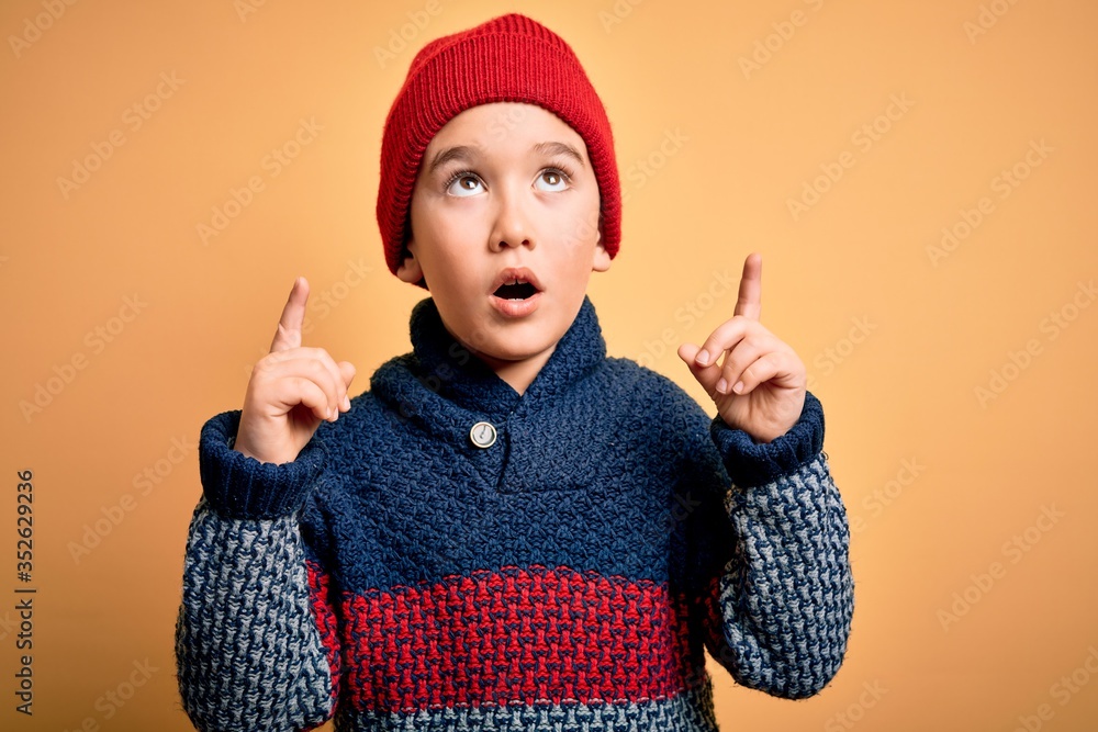 Young little boy kid wearing wool cap and winter sweater over yellow ...