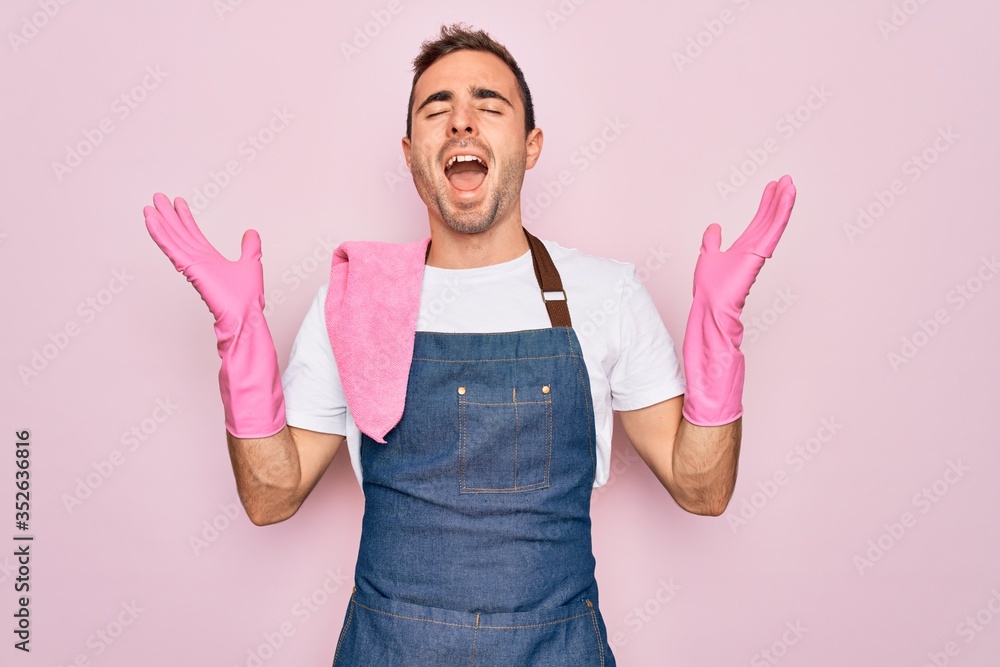 Young cleaner man with blue eyes cleaning wearing apron and gloves over ...