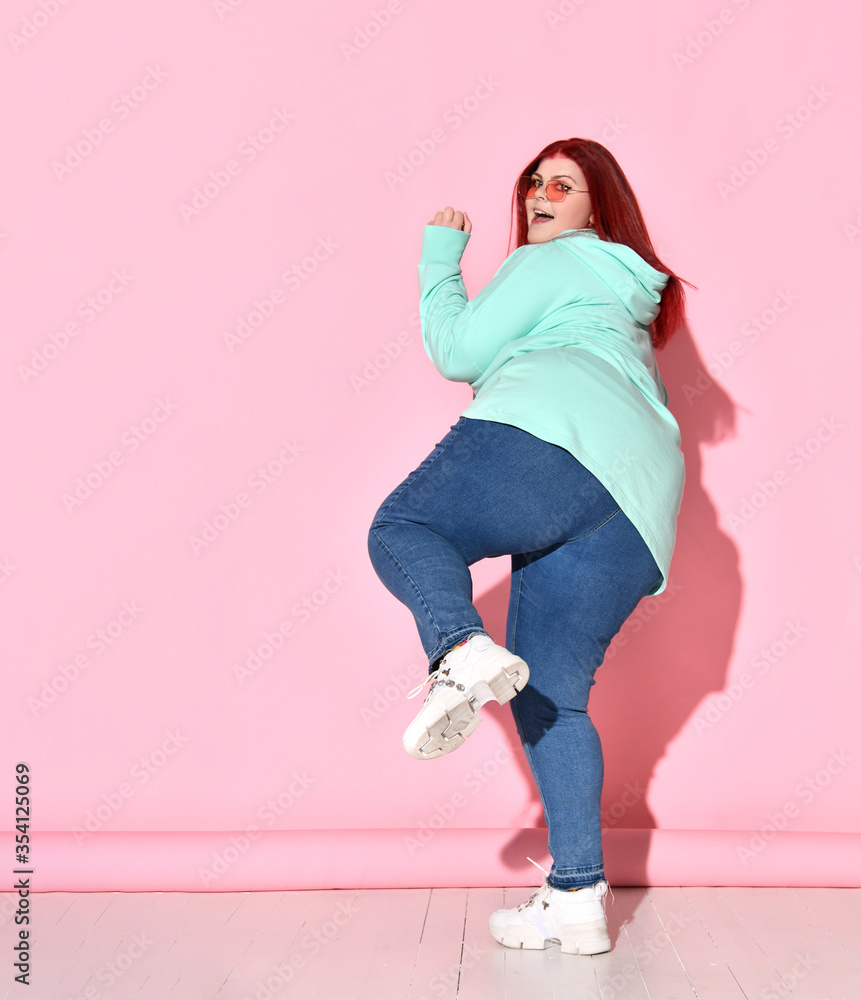 Pleasant fatty woman with long foxy hair posing on one leg looking over ...