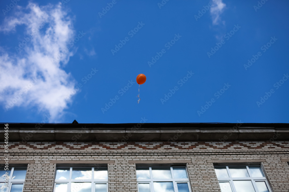 Orange balloon in the blue sky above the school. End of school year ...