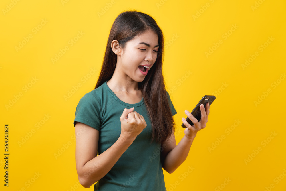 Shocked asian teenager in green tee shirt looking at mobile phone and ...