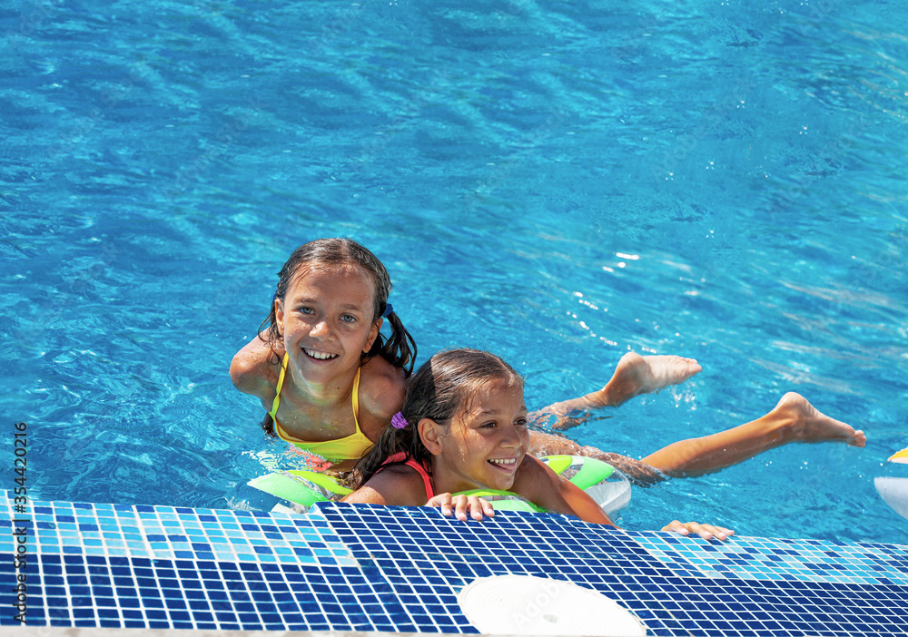 Two tween girls playing, splashing, laughing and have fun in the blue water of swimming pool ...
