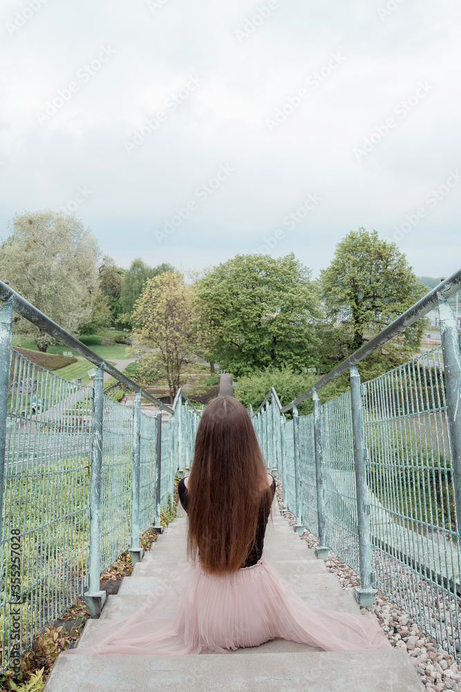 Girl sitting on the stairs in the park. Young woman in a pink skirt and ...