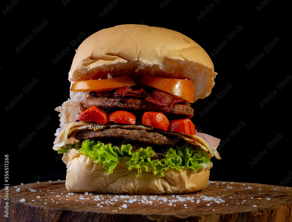 Big homemade burger with two beef burger, lettuce, tomato, sausage, ham ...