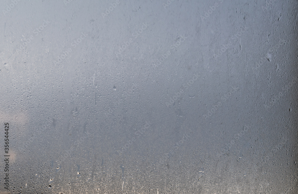 Morning rain drops on a glass window with blurred blue sky background ...