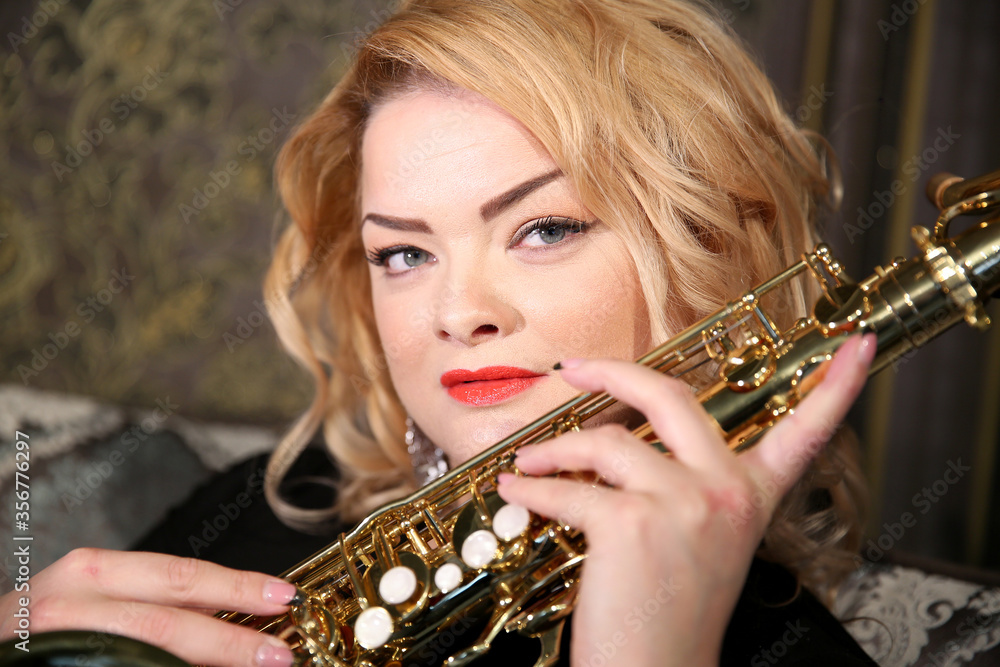 Portrait of a charming blonde with a saxophone in her hands. Beautiful ...