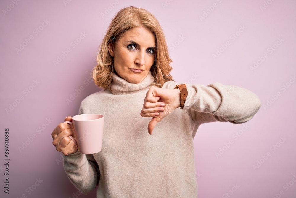Middle age beautiful blonde woman drinking pink mug of coffee over ...