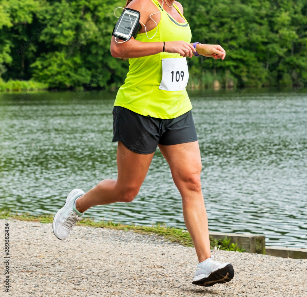 Runner with cell phone on arm running trail race next to a lake Stock ...