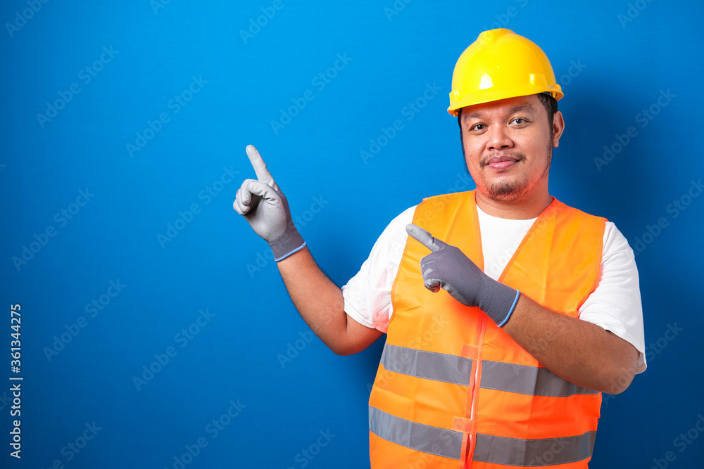 Fat Asian worker wearing a helmet presents something in his hand while ...