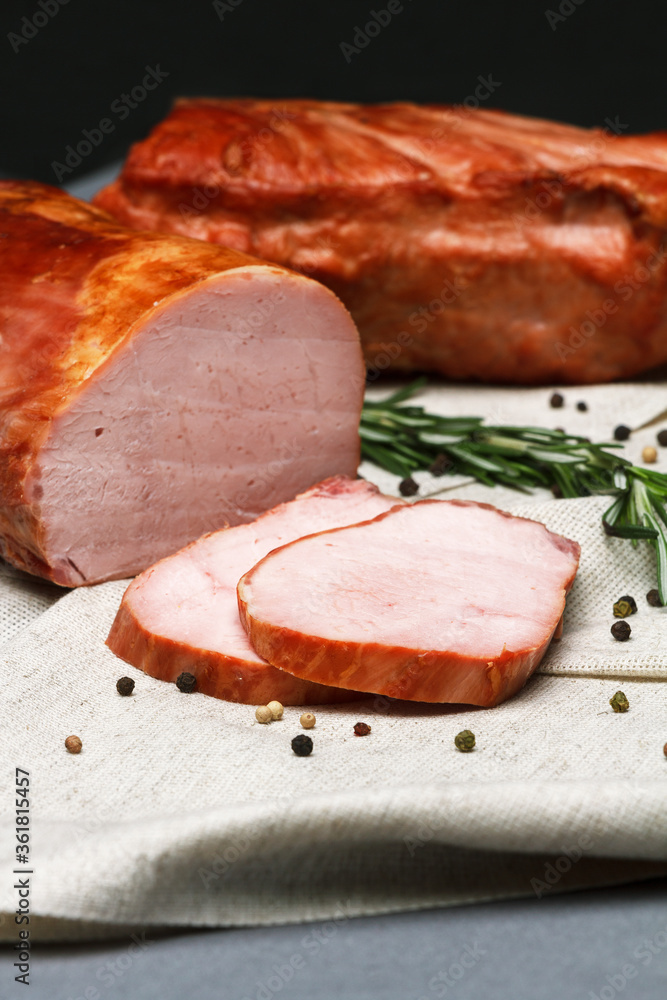 Sliced smoked ham lying on a rustic linen cloth, complete with black ...