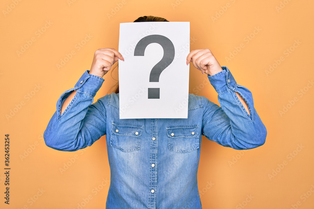 Woman covering face holding paper with question mark symbol. Standing ...
