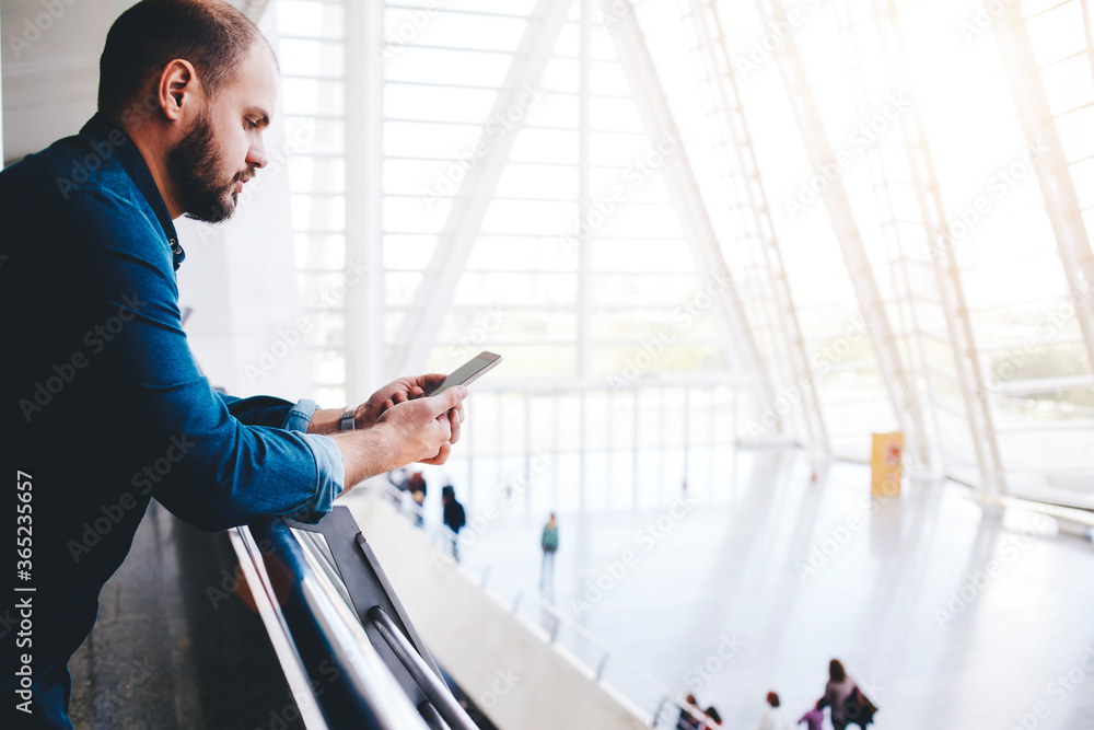 Handsome young man standing with mobile phone on second floor of modern ...