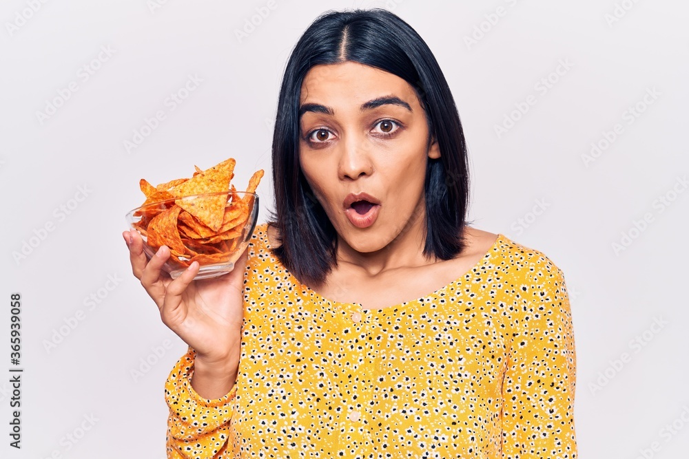 Young beautiful latin woman holding nachos potato chips scared and ...