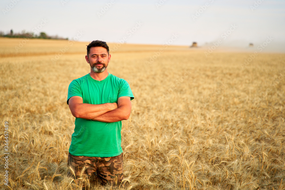 Happy farmer proudly standing in wheat field with arms crossed on chest ...