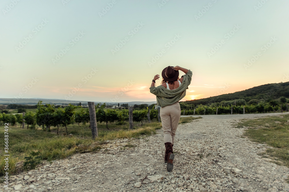 Girl in a cowboy hat at sunset in the countryside in the vineyards ...