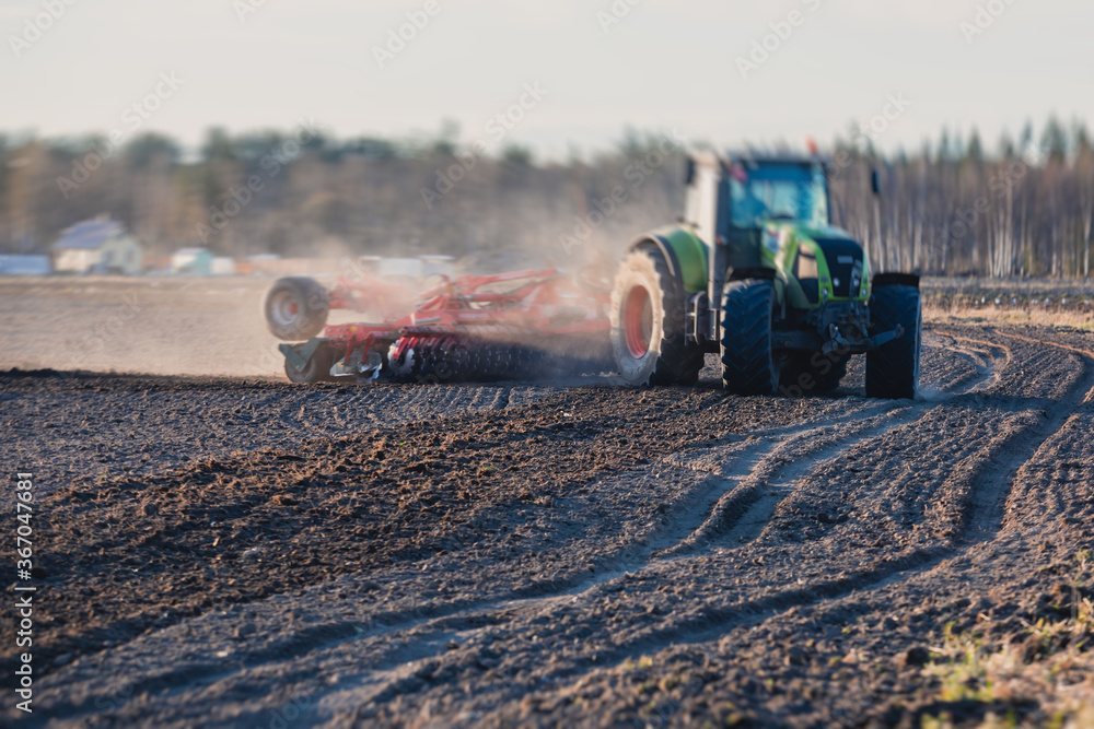 Tractor with a disc harrow system harrows the cultivated farm field ...