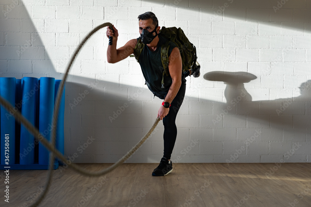 Battle ropes workout with extended leg and training mask. Indoor on oak ...
