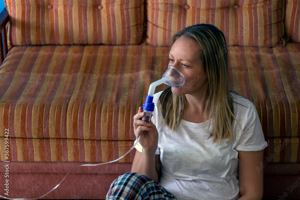 Young woman doing inhalation with nebulizer at home.Female holding a ...