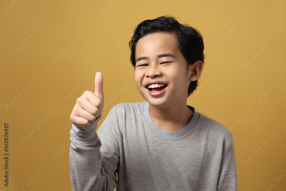 Happy Asian boy smiling at camera and showing his thumb up, OK good ...
