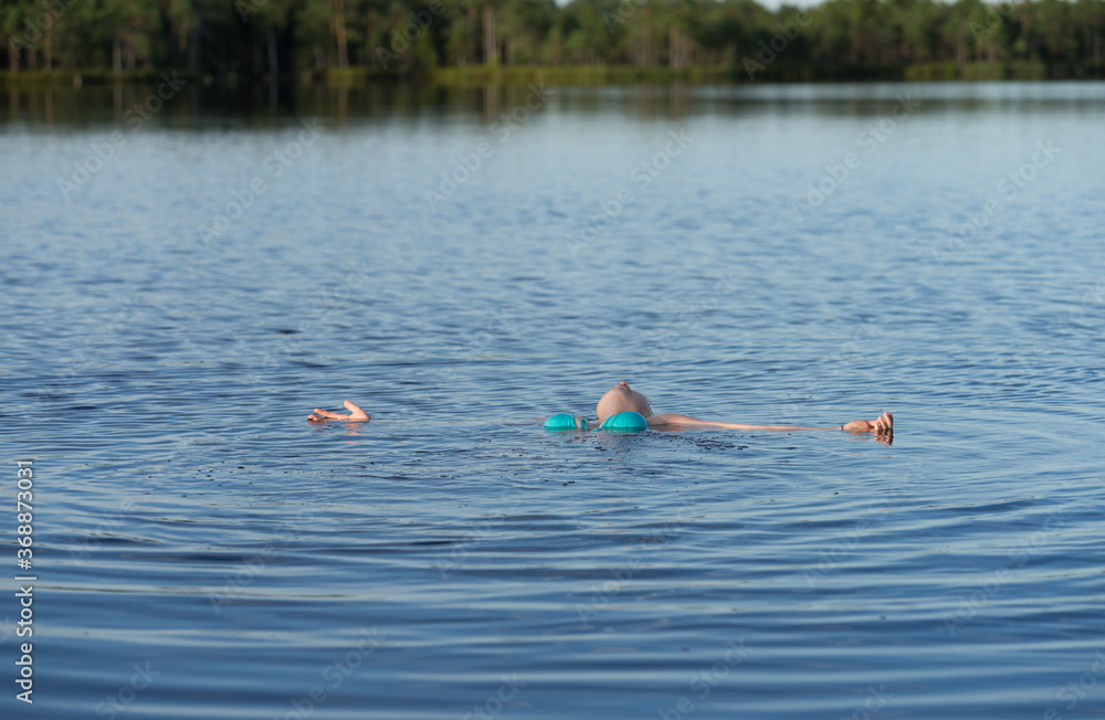 Teenager blonde girl swimming in bog lake. Hands and feet spread out ...
