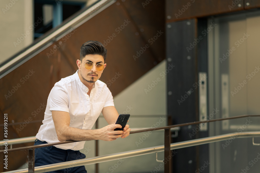 Urban portrait of young syrian man holding his mobile phone standing on ...