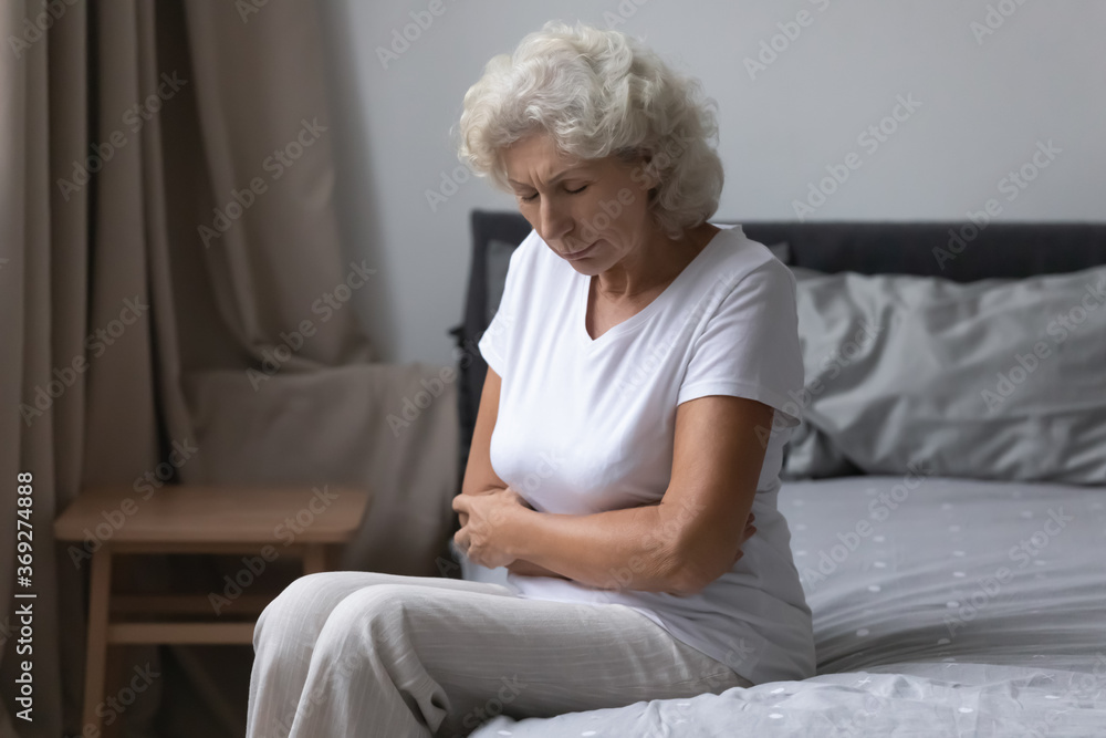 Unhealthy senior grey haired woman awakened woke up sit on bed in ...