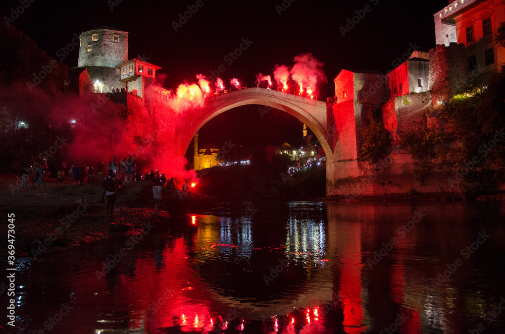 People holding red flares on bridge during night show. The Old Bridge ...