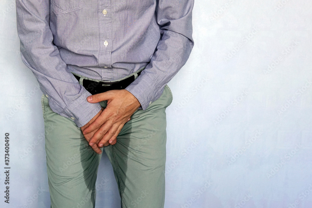adult man holds hands the groin area and trousers wet from urine ...