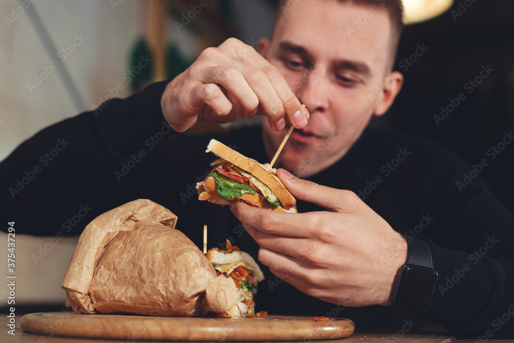 Handsome man sitting in a restaurant and eating club sandwich. He is ...