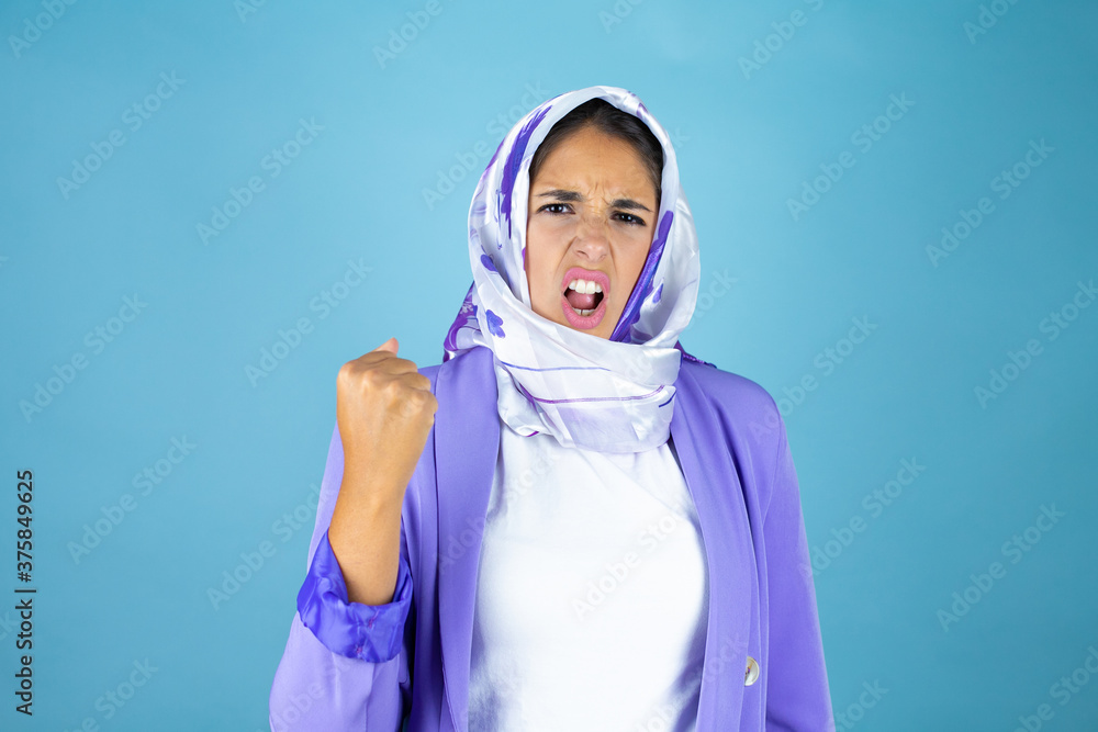 Young beautiful arab woman wearing islamic hijab over isolated blue ...