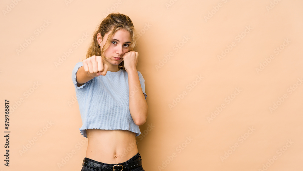 Young caucasian woman isolated on beige background throwing a punch ...