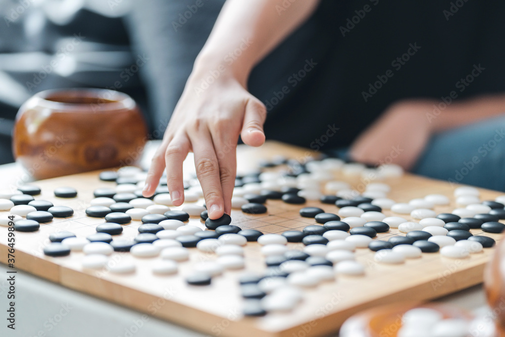 Foto de Stock hand putting baduk black stone on wooden grid board - an ancient game also known ...