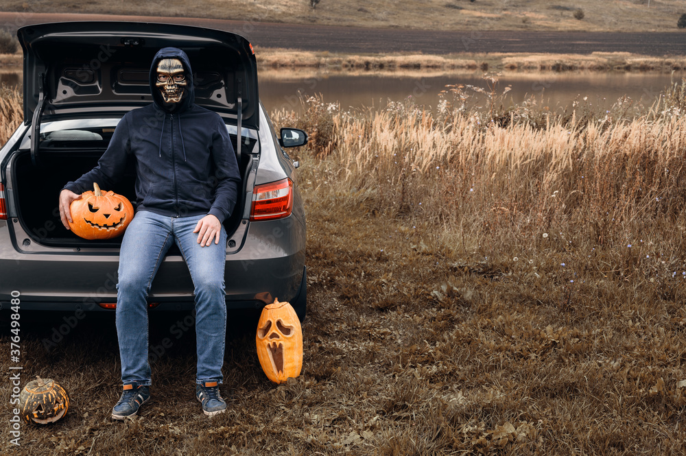 An unrecognizable adult man wearing a skull mask sits in the trunk of a ...