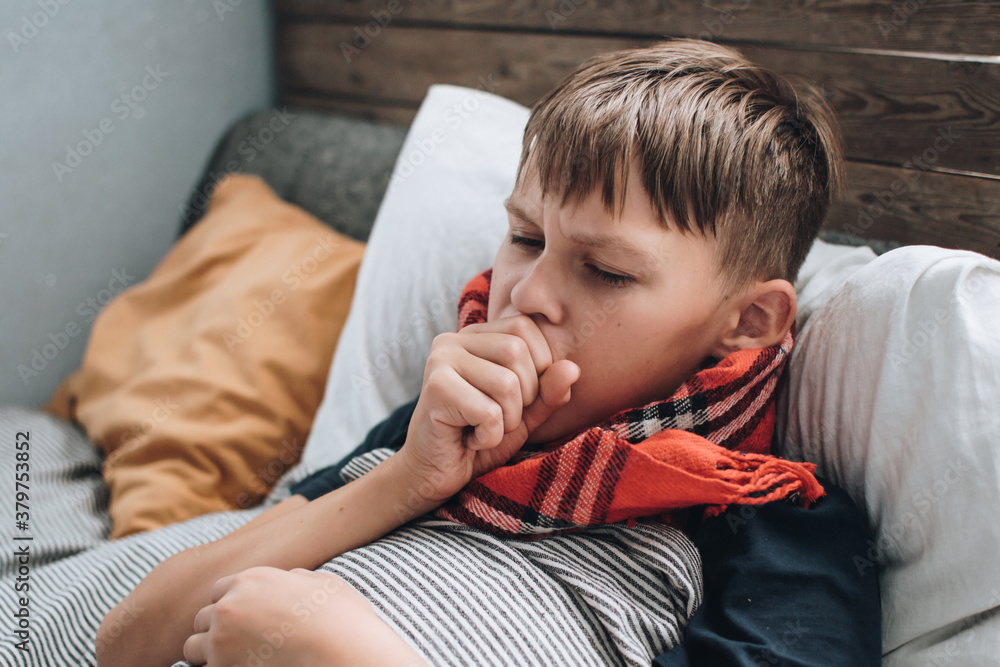 Sick teenage boy with flu is sneezing and coughing on the bed ...