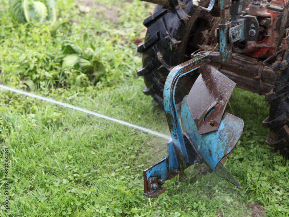 Auxiliary plow on Walk-behind tractor washing with water flow on green ...