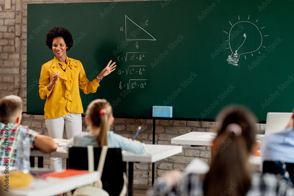 Happy African American math teacher explaining lecture on blackboard in ...